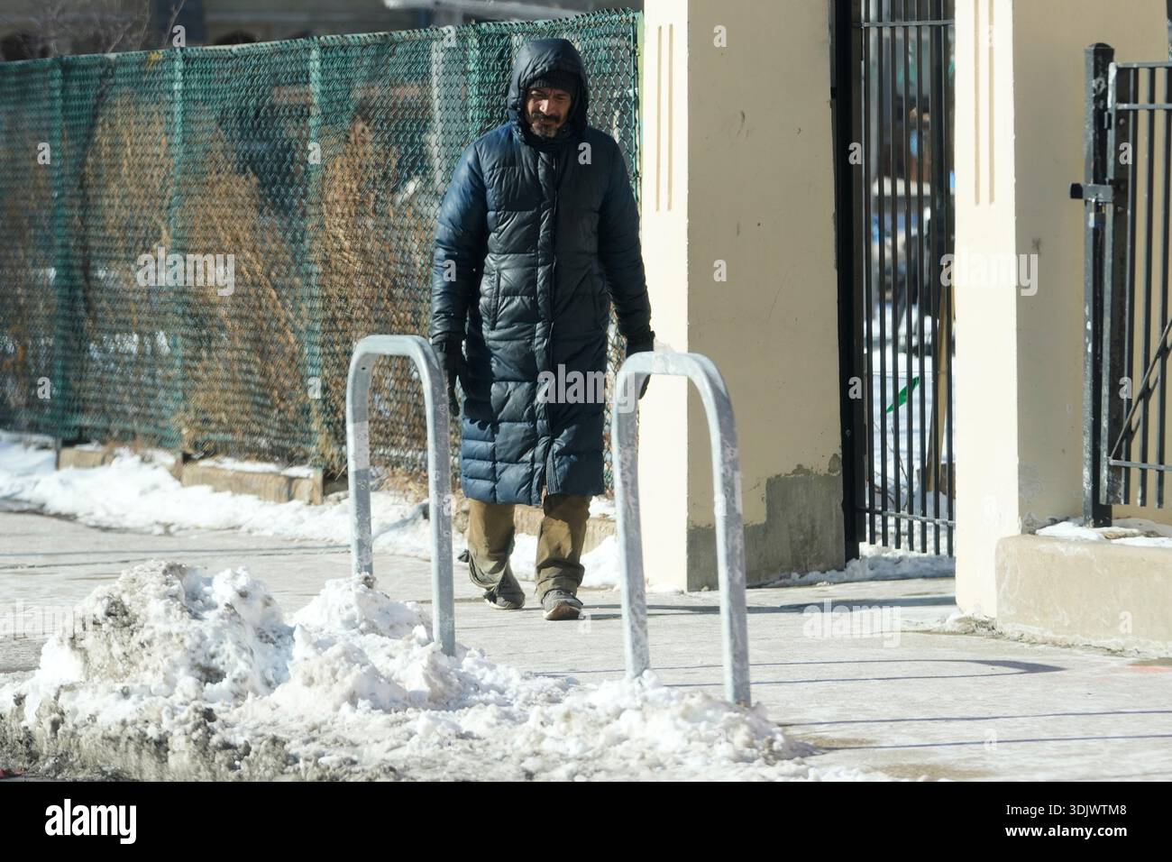 A pedestrian bundles up as walks on a sidewalk during a cold day in ...