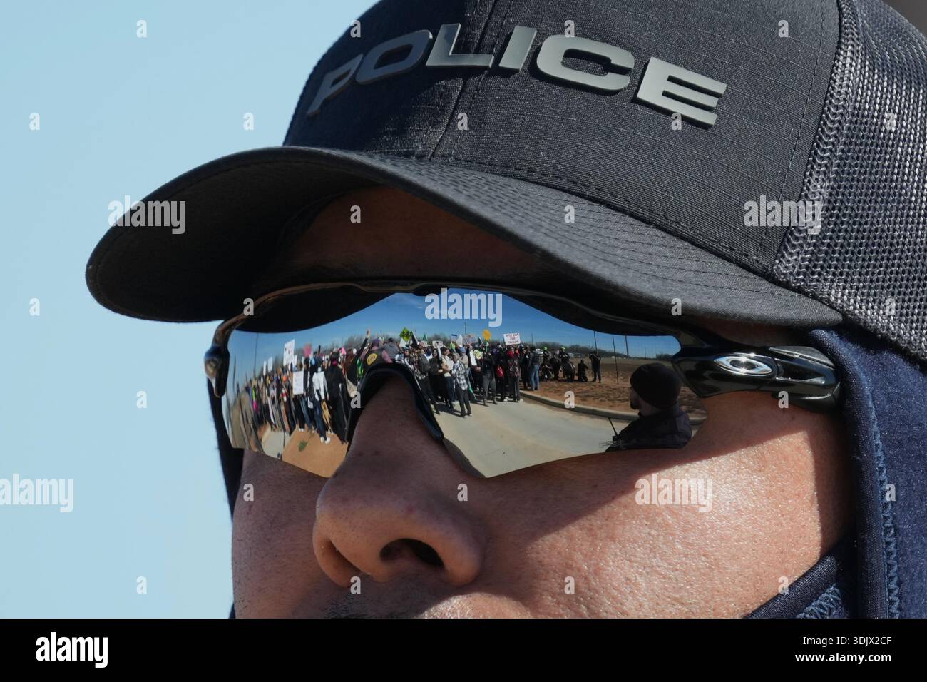 A police officer watches protesters, reflected in his sunglasses ...