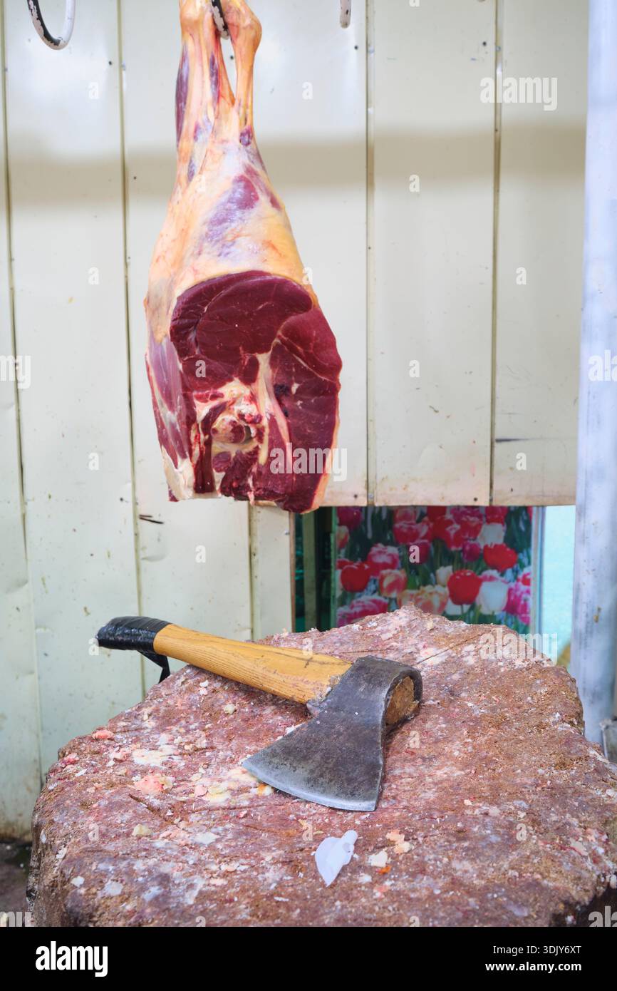 A fresh leg of beef at a butcher with wood chop block and axe. At the ...