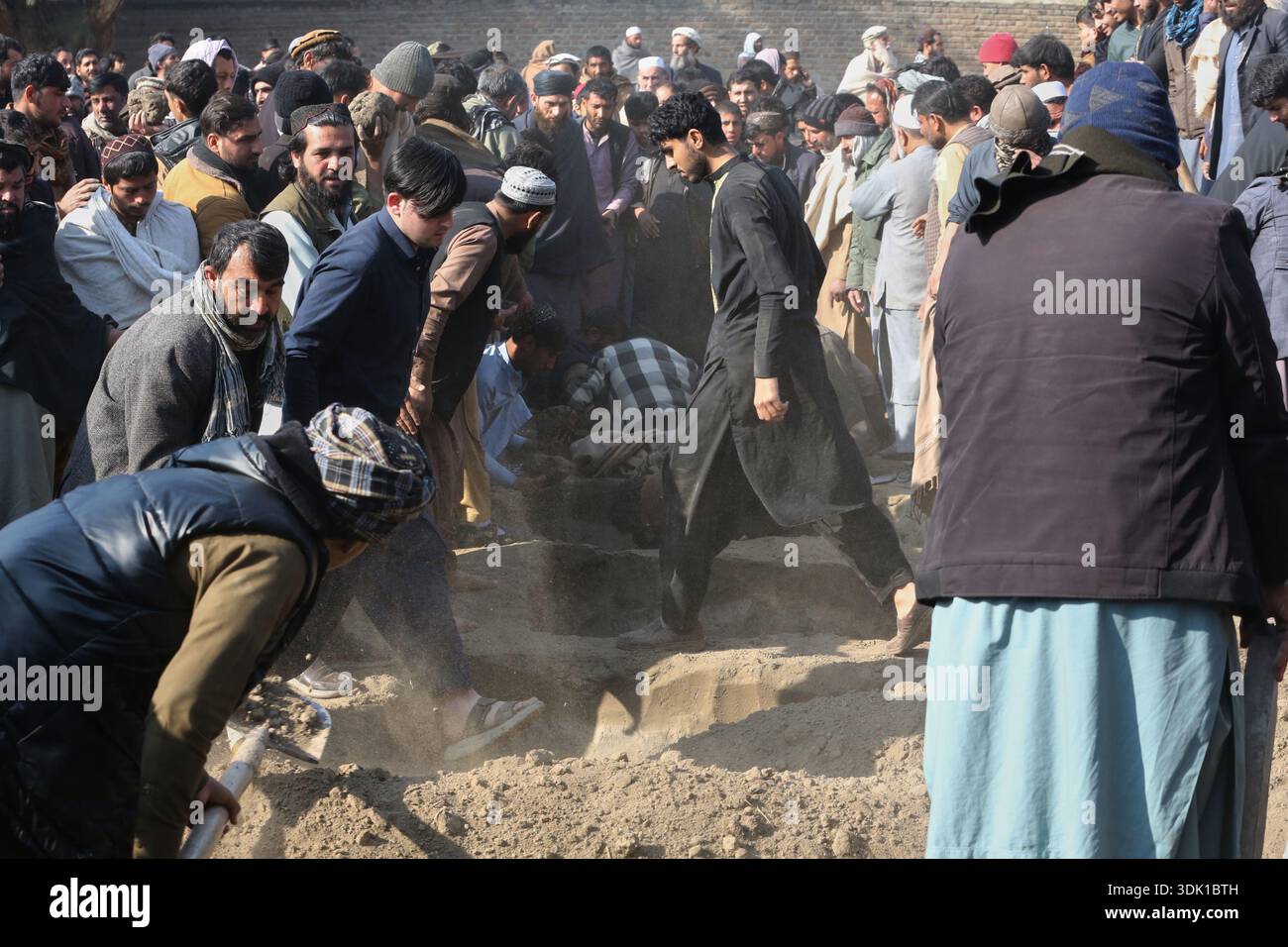Mourners shovel dirt into a grave during a burial of victims of a house ...