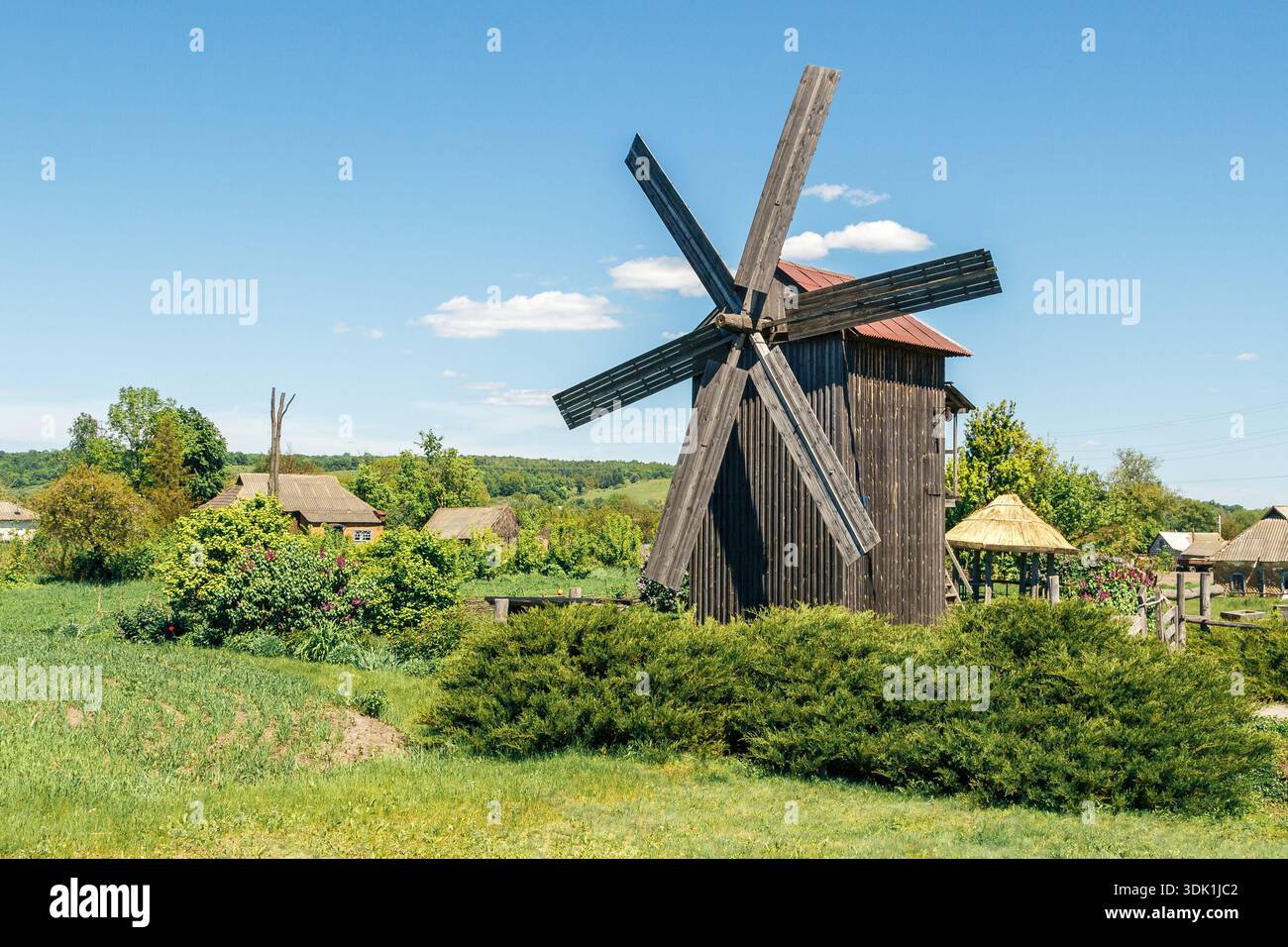 Old wooden windmill standing in sunny countryside with village houses ...