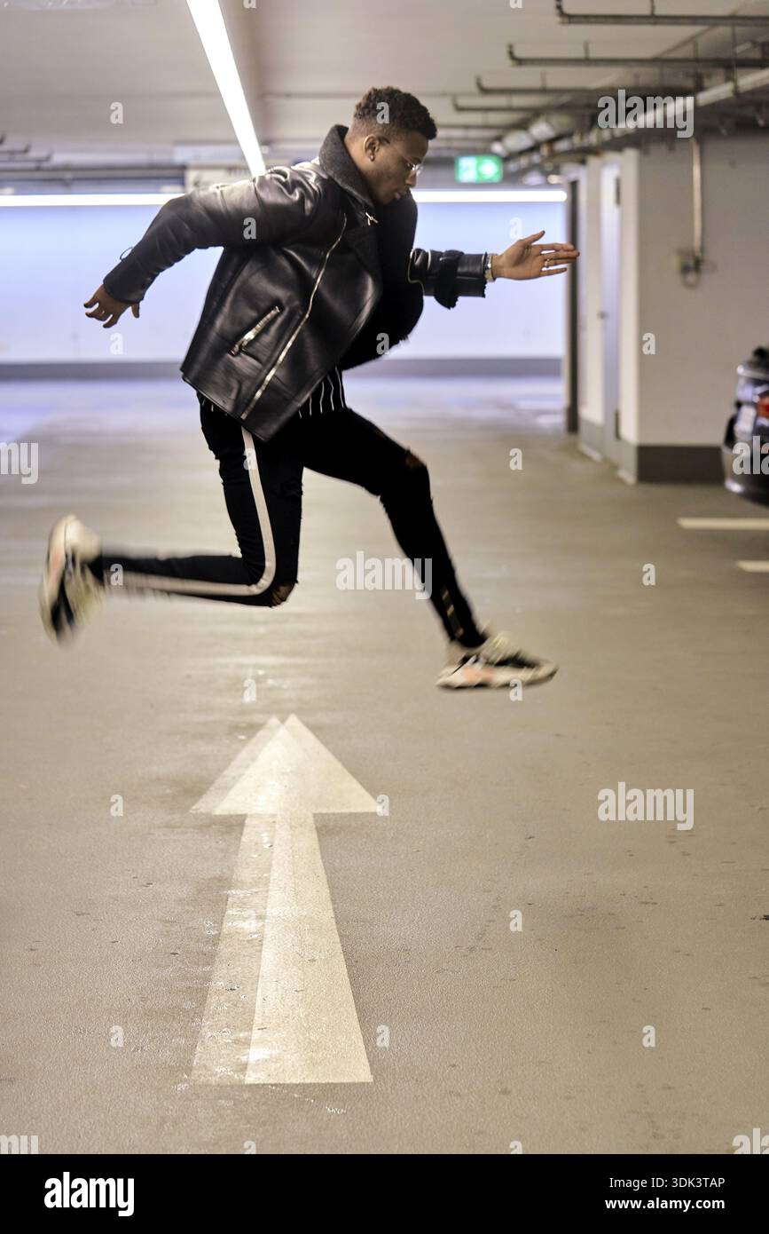 African man jumping forward in parking garage, Person energetically ...