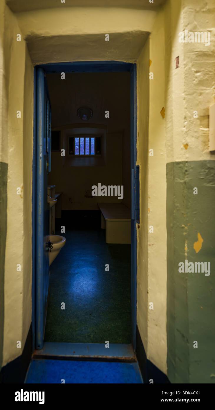 Open blue door leading into a small prison cell with barred window ...
