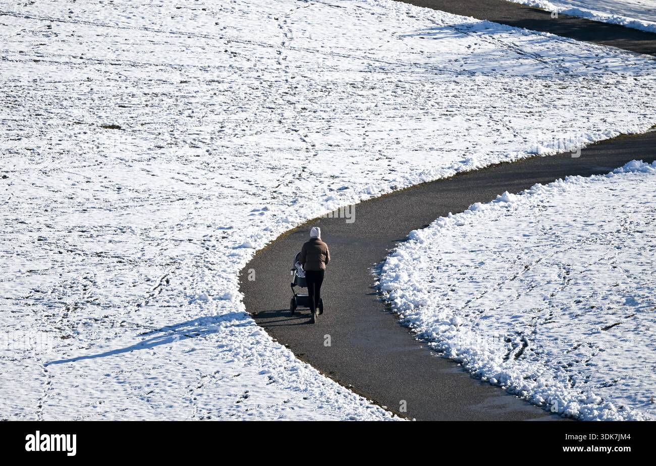 30 January 2026, Bavaria, Munich: A woman with a baby carriage takes ...
