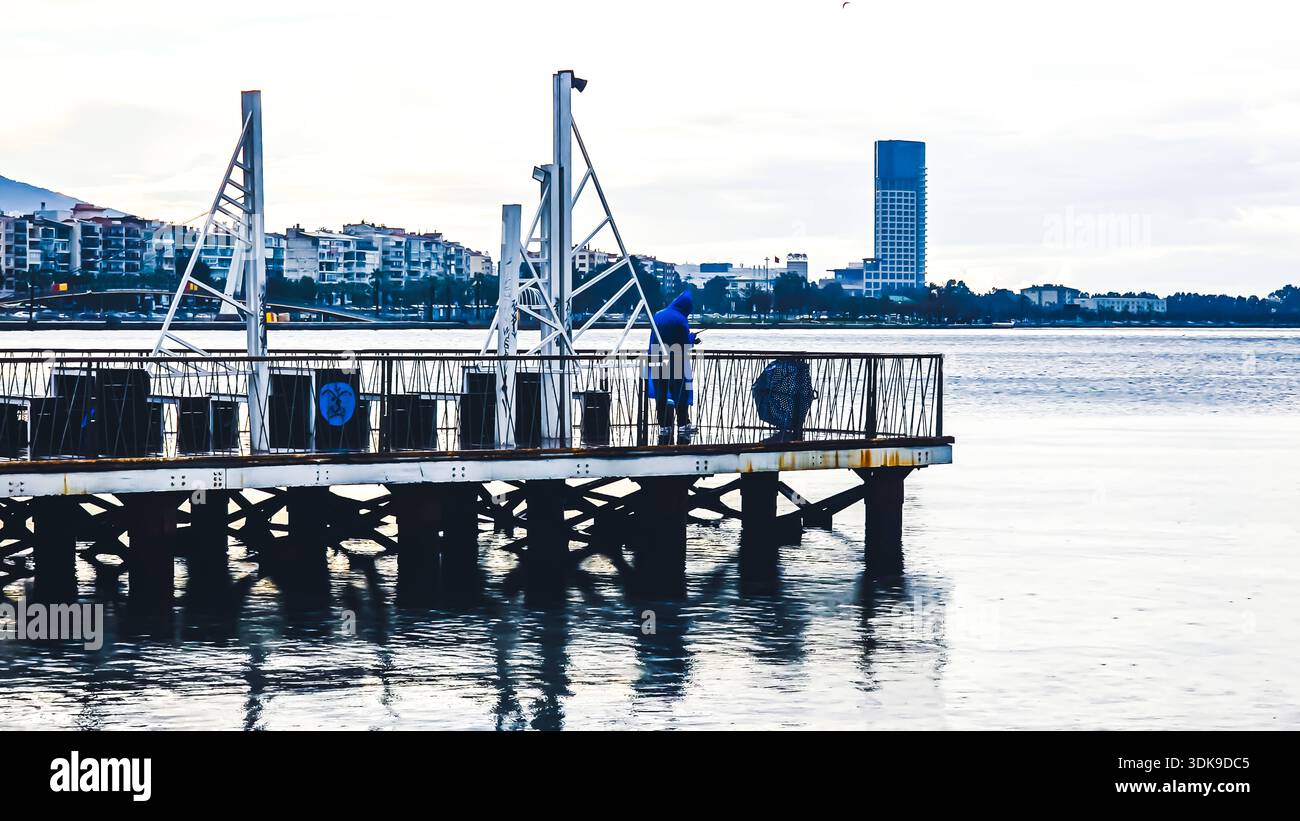 A lone fisherman A lone fisherman wearing a blue hooded raincoat stands ...