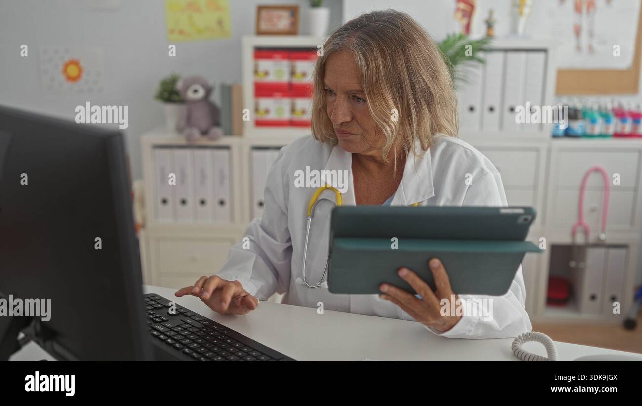Senior woman pediatrician holds tablet and taps screen while typing at ...