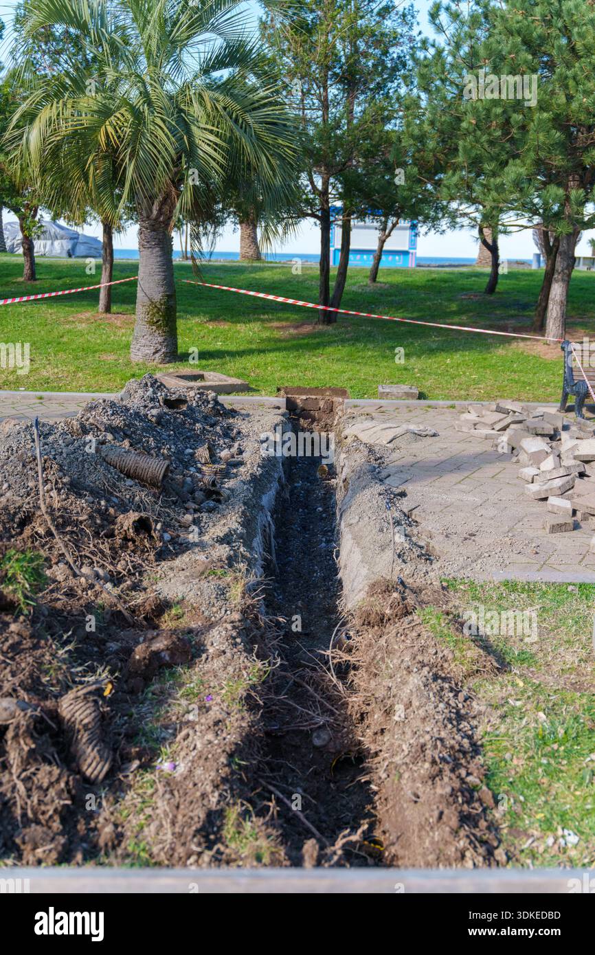 Trench dug through park walkway with tubing, debris, and caution tape ...