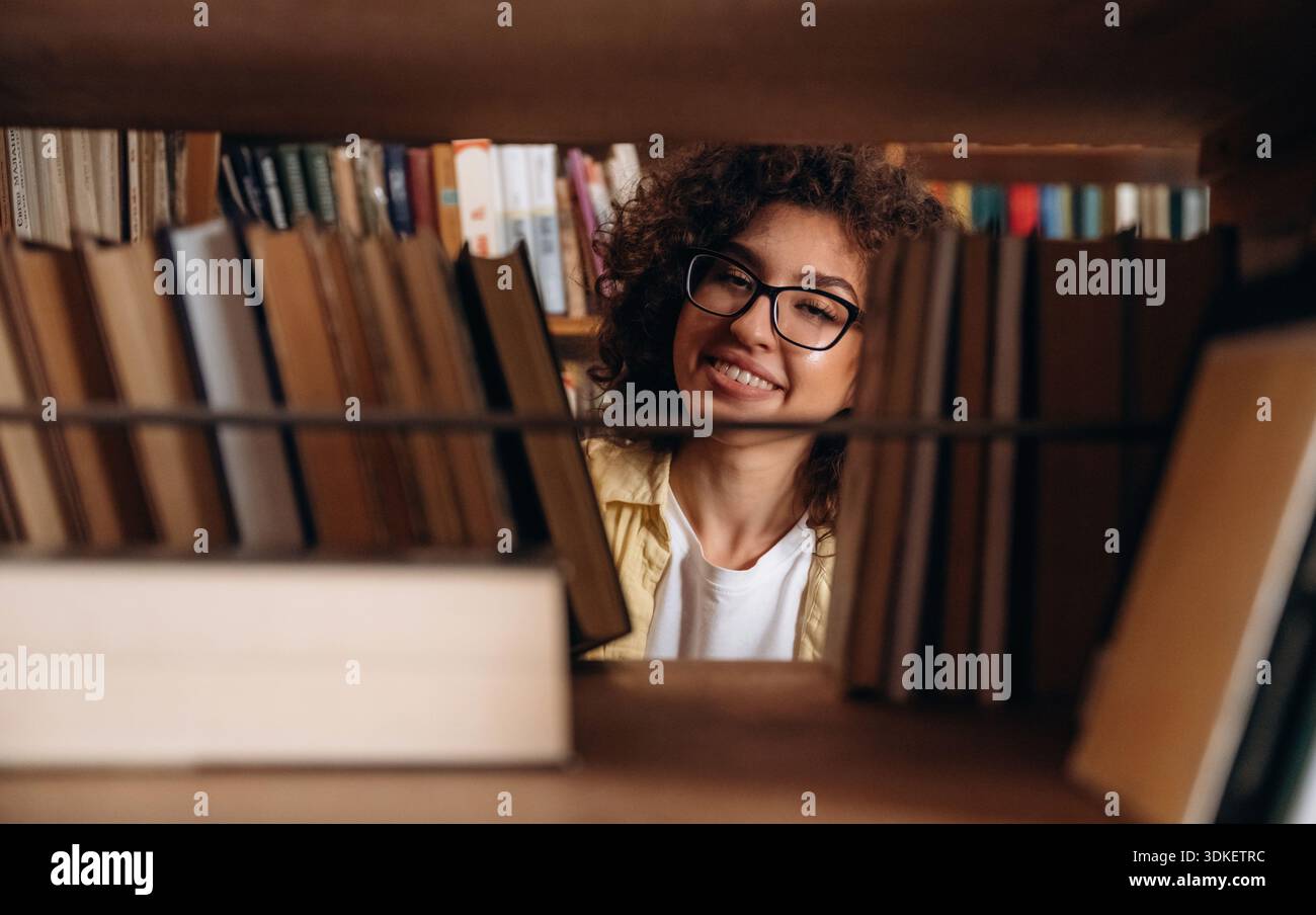 Searching for the right book, view through the shelf. Beautiful woman ...