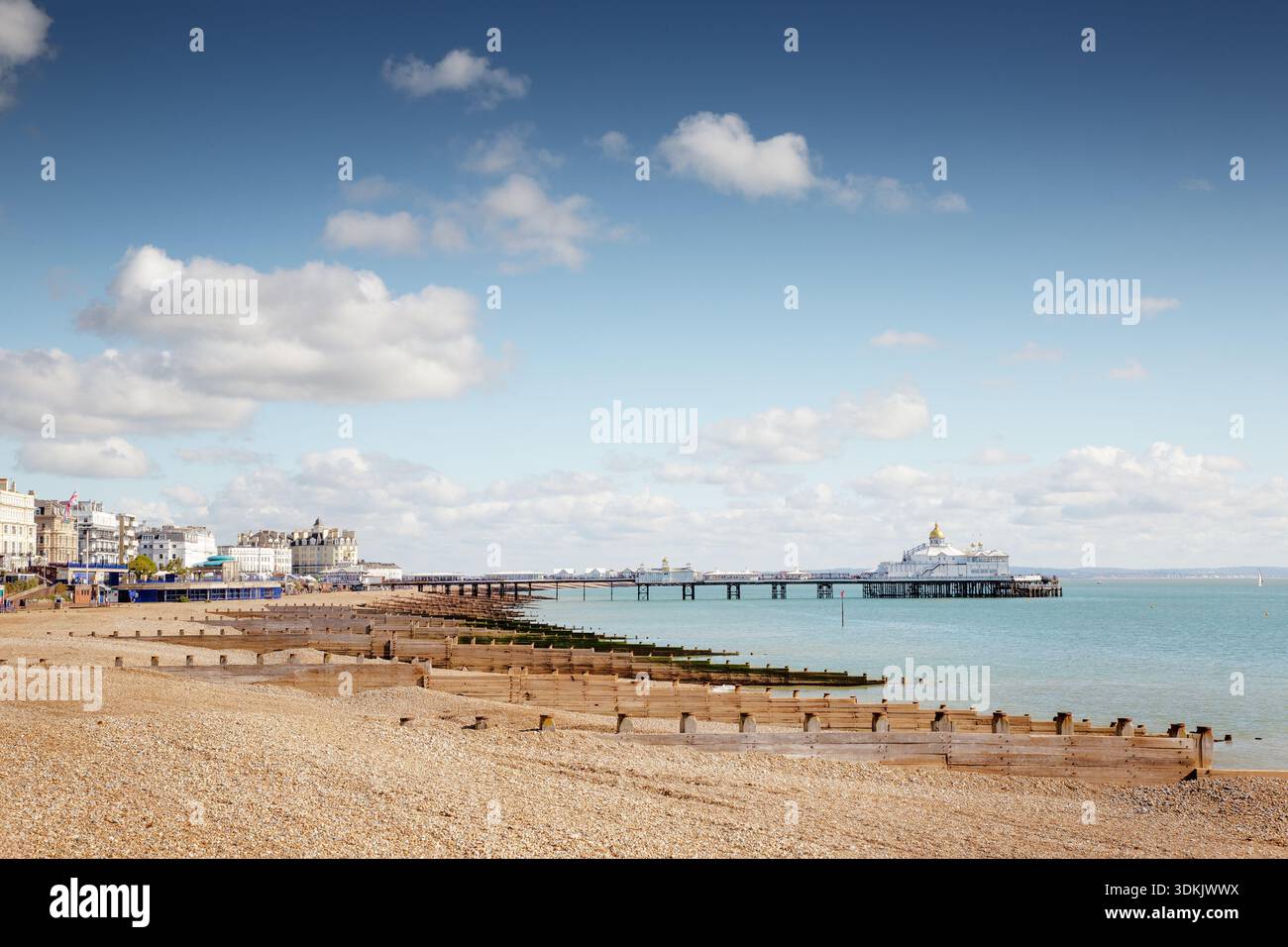 Bright seaside scene with a pebble beach, groynes, and a long pier ...