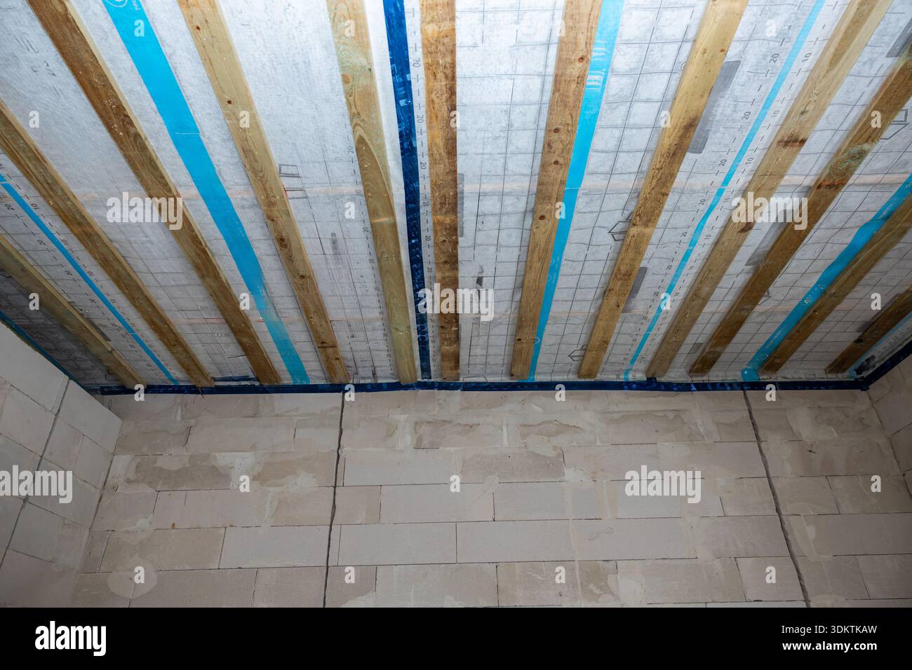 Unfinished ceiling with exposed wooden beams and blue insulation strips ...