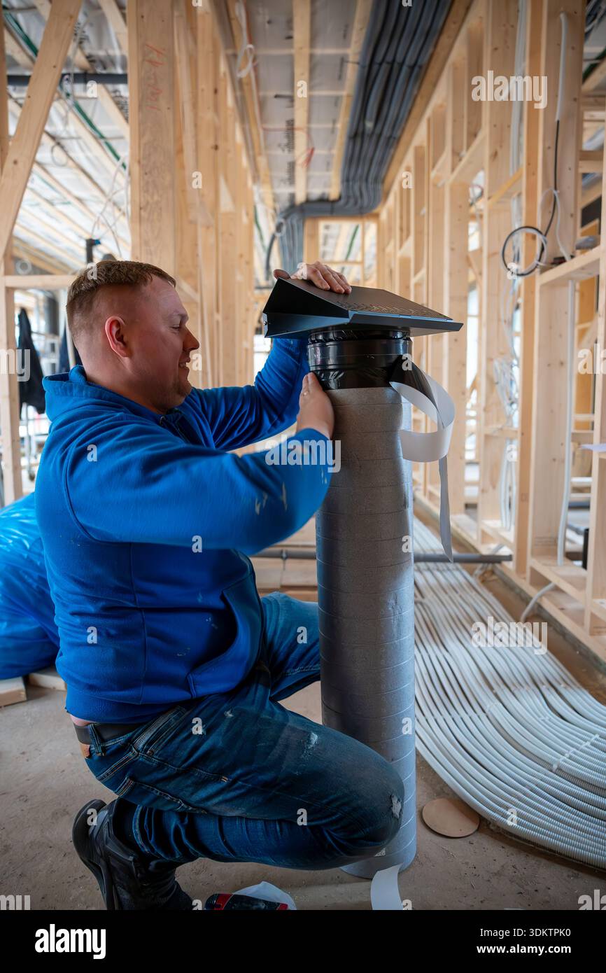 A worker in a blue hoodie secures insulated ductwork in a house under ...