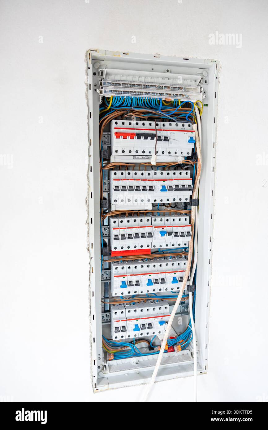 An open electrical panel embedded in a white wall, showing rows of ...