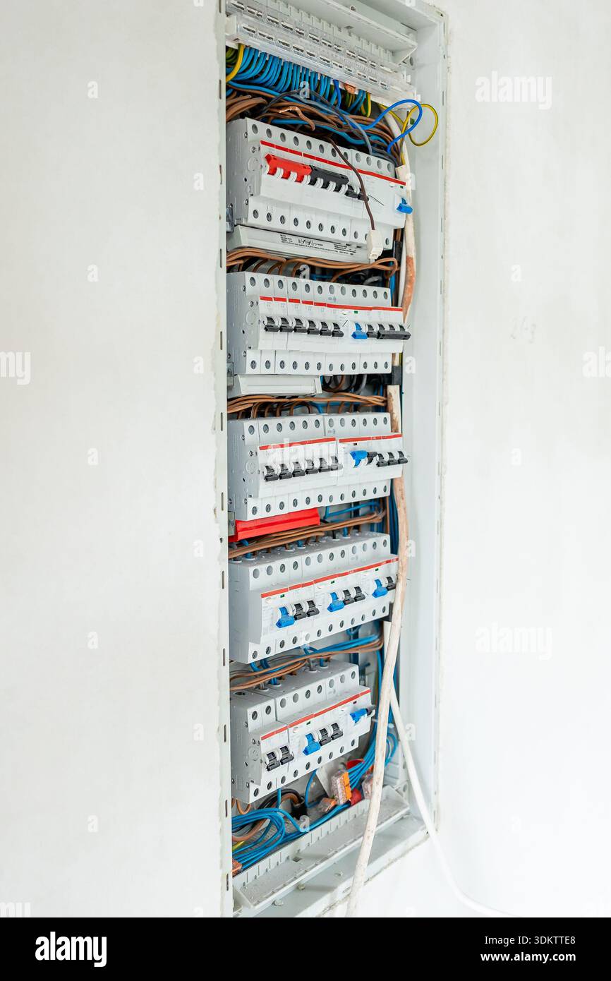 An open electrical panel in a white wall shows organized rows of ...