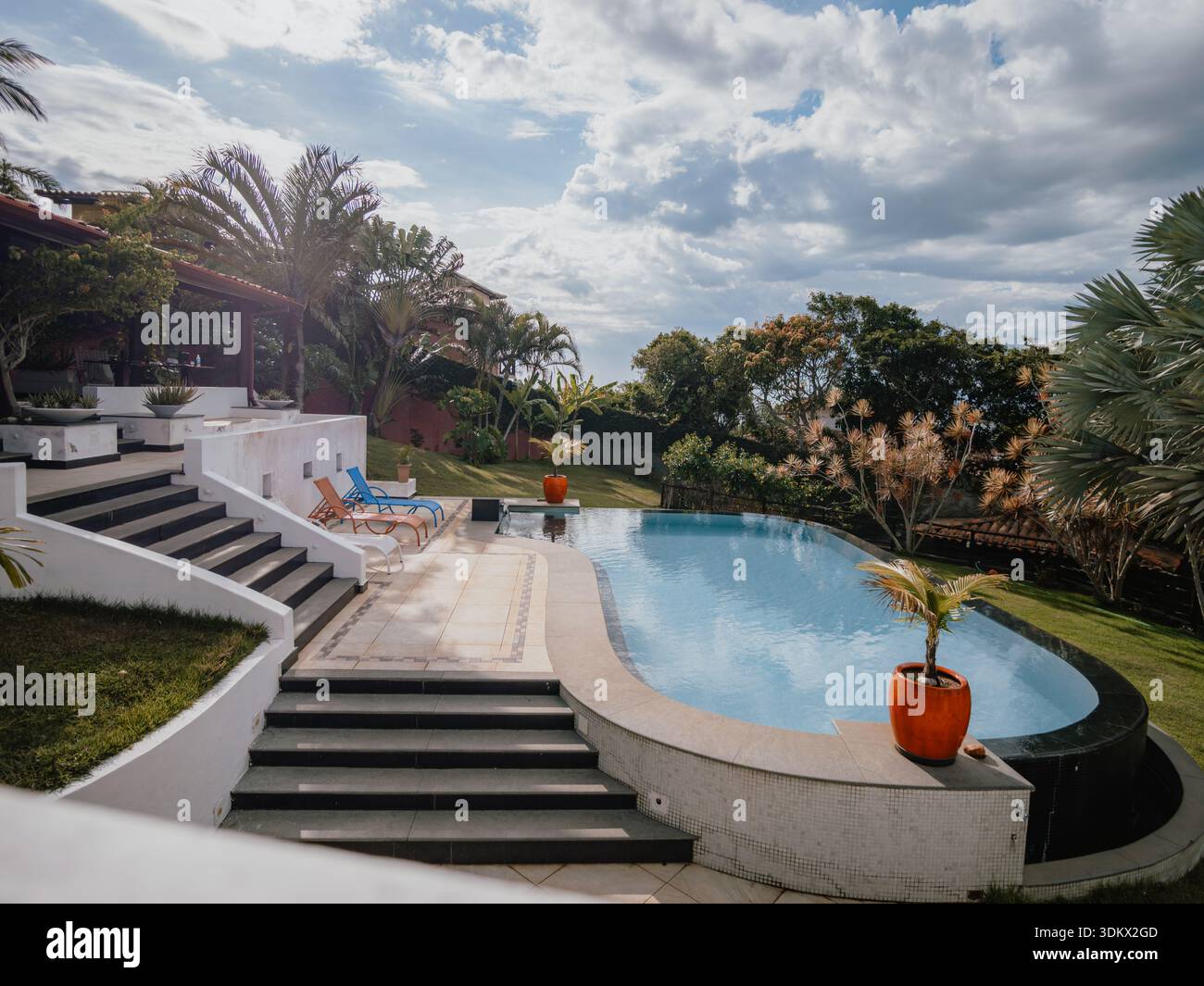 Curved outdoor pool with stairs, rest area and vegetation around, under ...