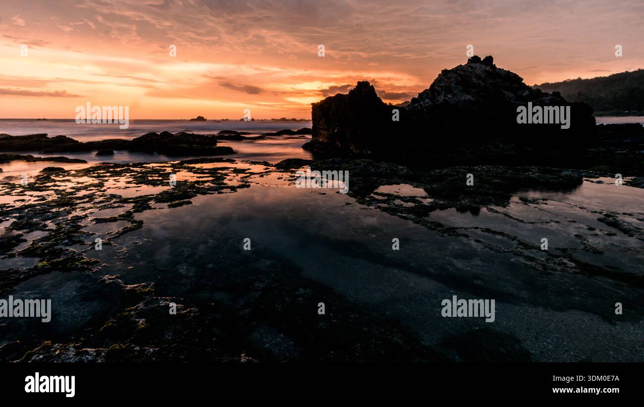 Dramatic sunset sky with vibrant clouds and big coral as sillhouettes ...