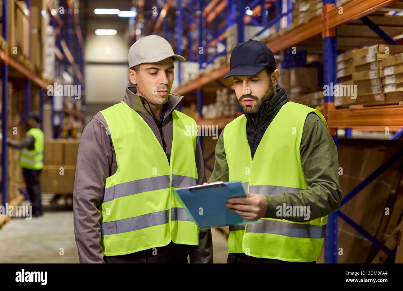 Two warehouse workers reviewing inventory checklist on clipboard among ...