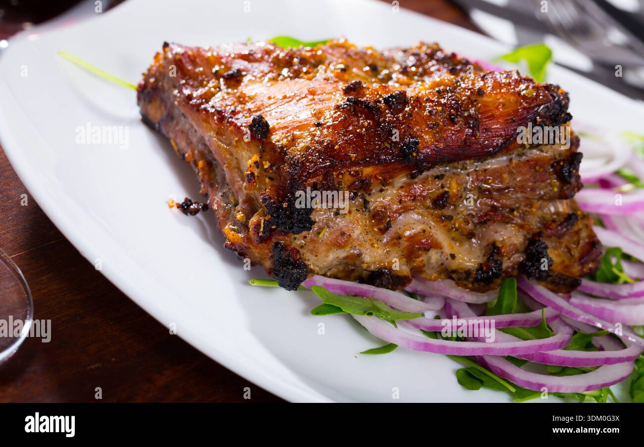 Juicy barbecue rack of pork served on fresh arugula with onion rings ...