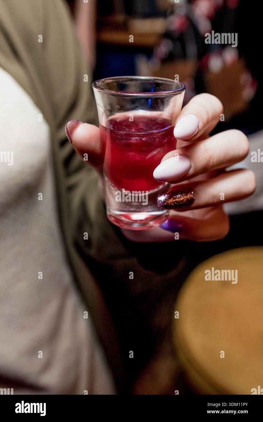 Young woman holding glass cup with alcoholic cocktail in her hand in ...