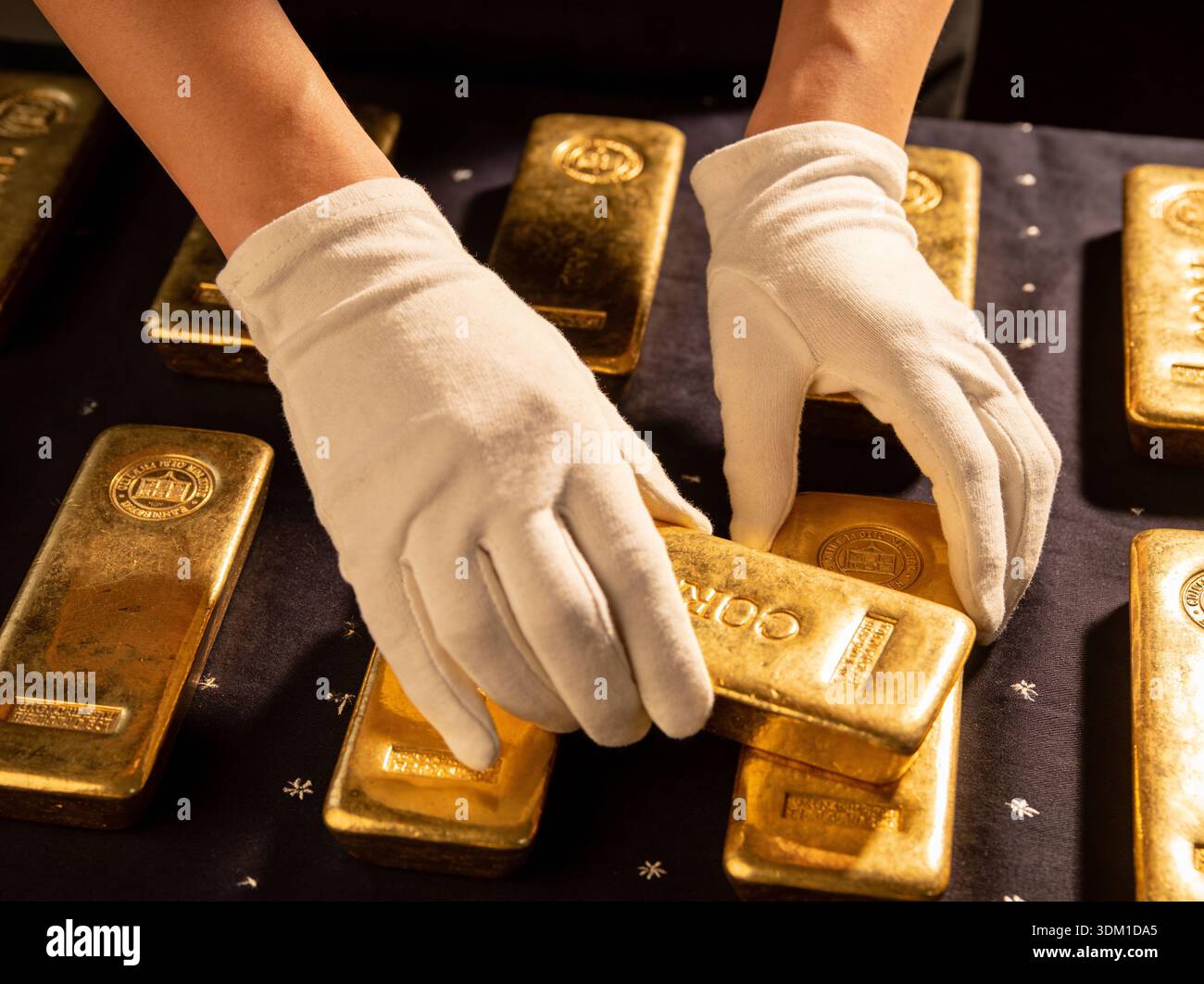 A person is wearing gloves and touching a gold bar. The gold bars are ...