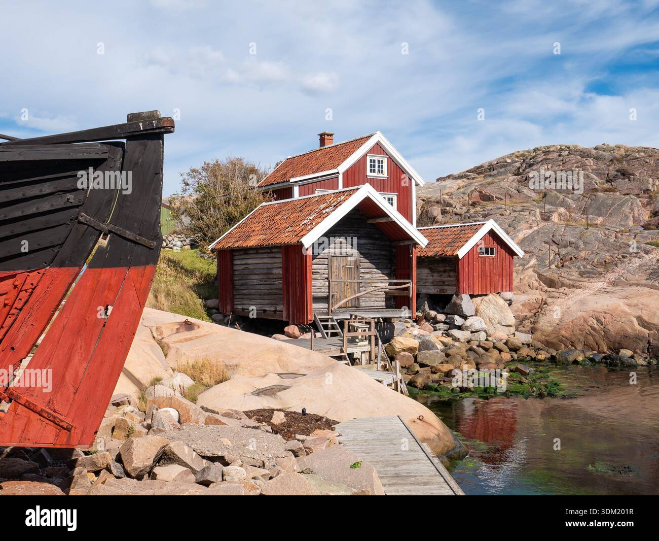 Traditional wooden boathouses beside granite rocky shoreline in Lysekil ...
