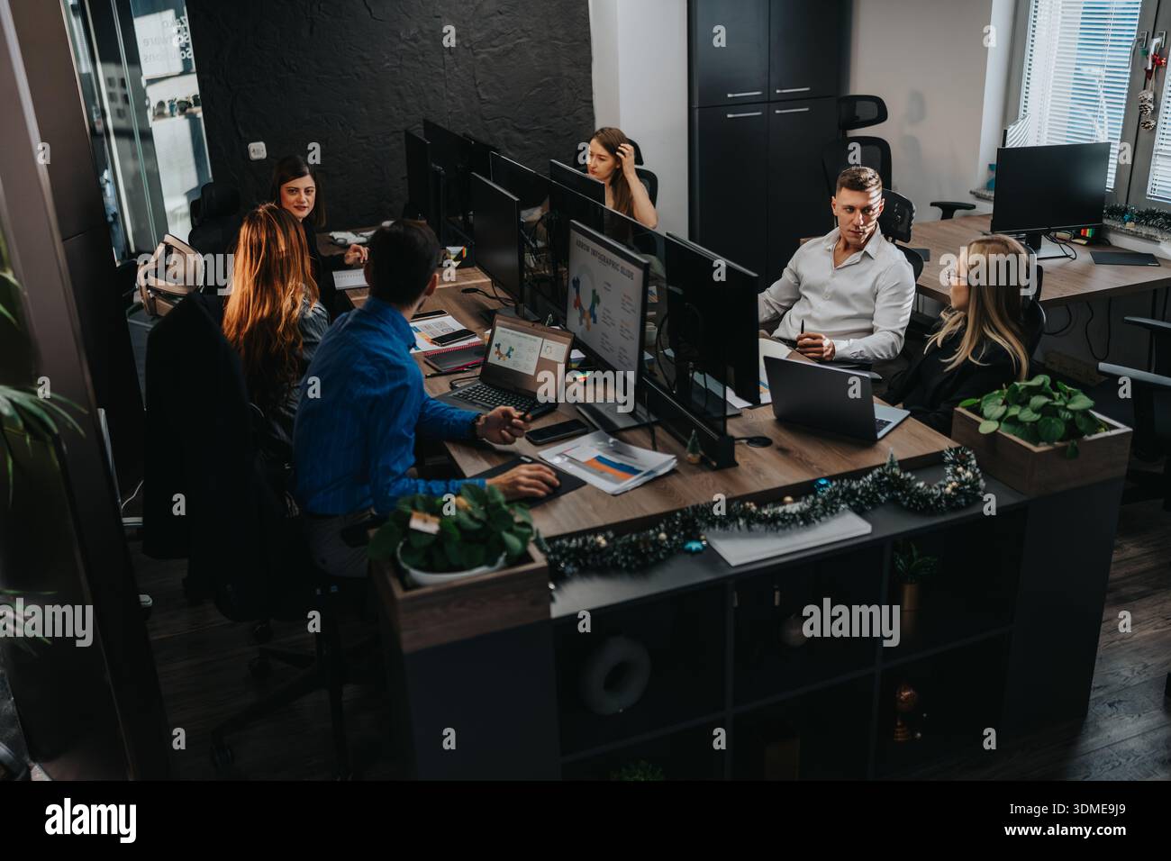 Modern office team at a shared desk with multiple screens, festive ...