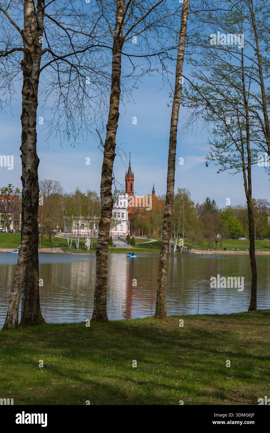 Birch trees frame calm water in Druskininkai, Lithuania. A red brick ...
