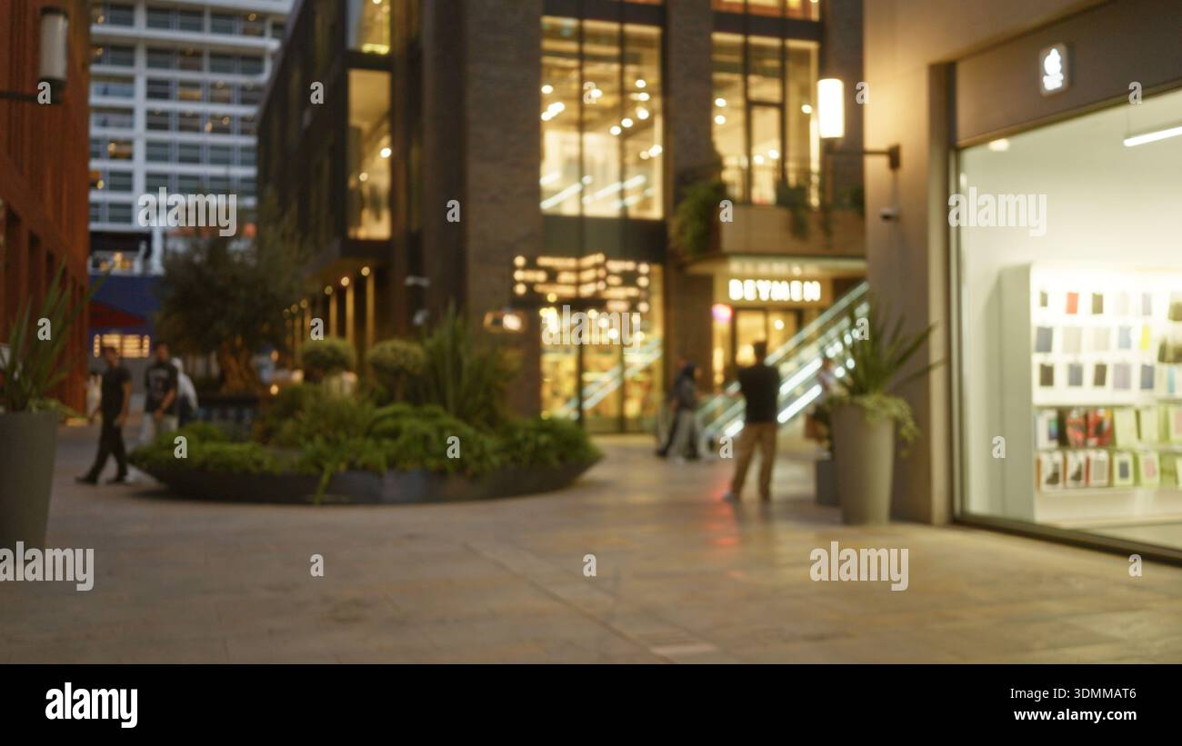 Blurry urban shopping plaza with defocused storefronts, planters and ...