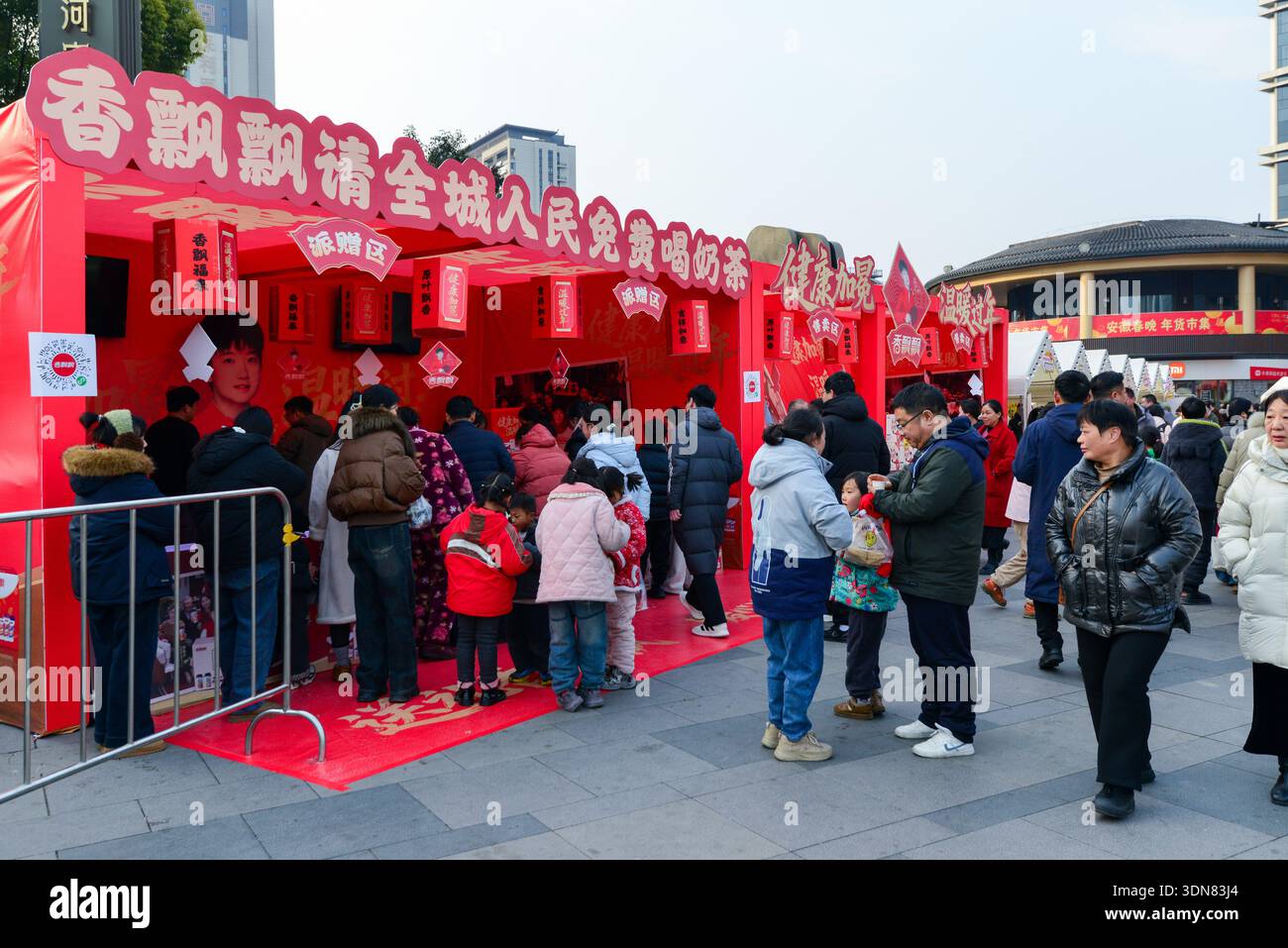 A large crowd queues up at a red-themed booth offering free milk tea ...