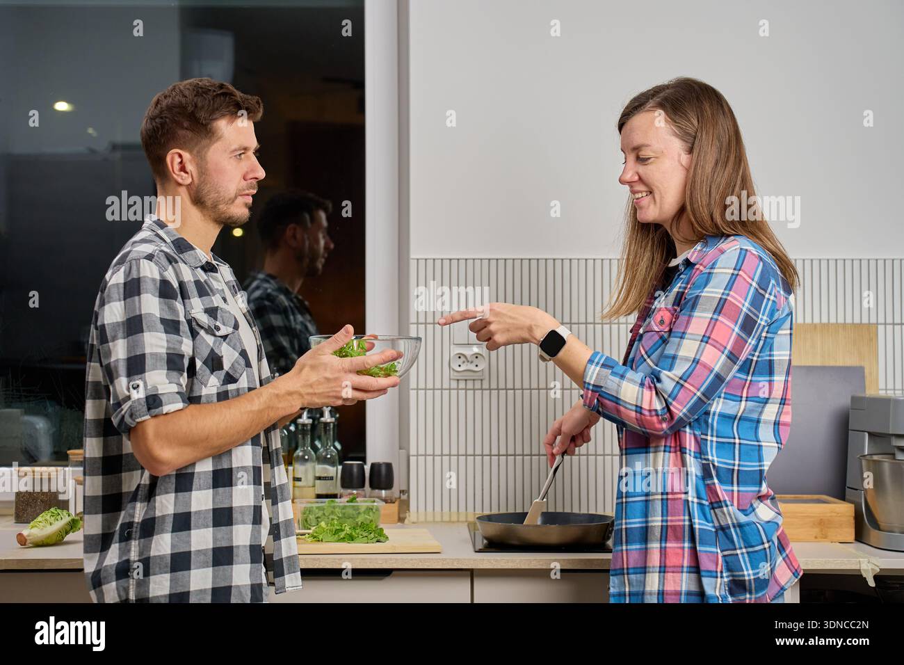 Man holding bowl of salad and woman cooking in pan while talking in ...