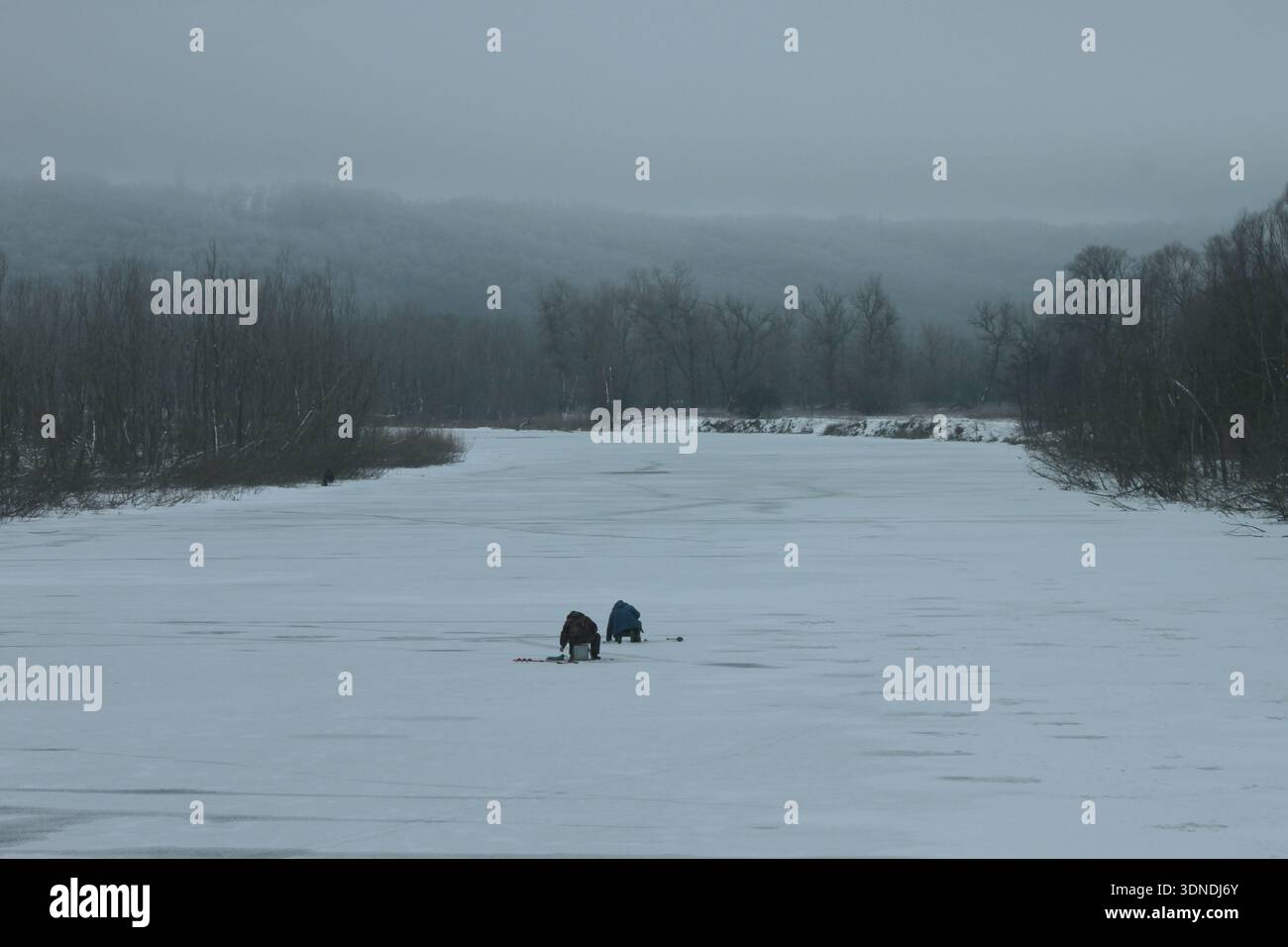 two fishermen ice fishing on a frozen lake in cloudy weather Stock ...