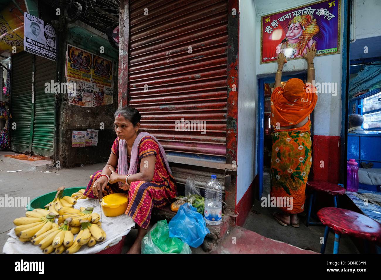 A Bangladeshi Hindu woman prays at a temple as another sells banana on ...