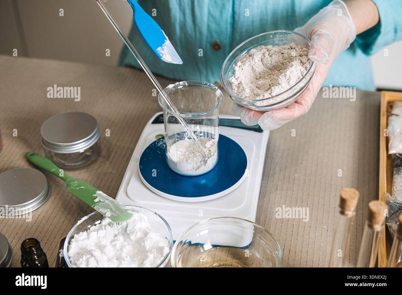 Hands use blue spatula to transfer white powder from bowl into glass ...