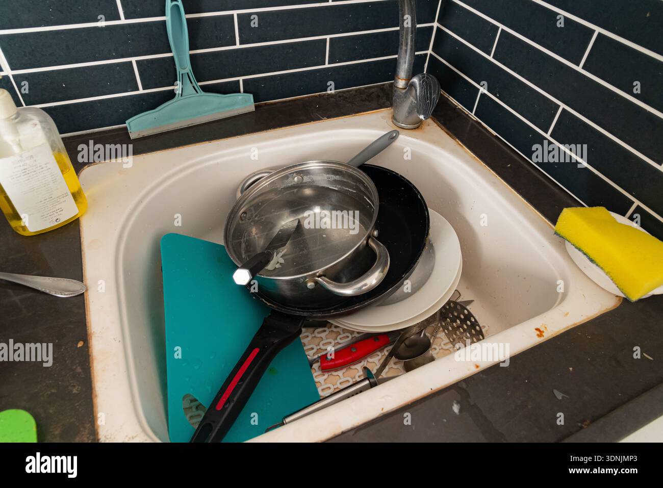 Dirty kitchen sink filled with unwashed dishes, utensils and cleaning ...