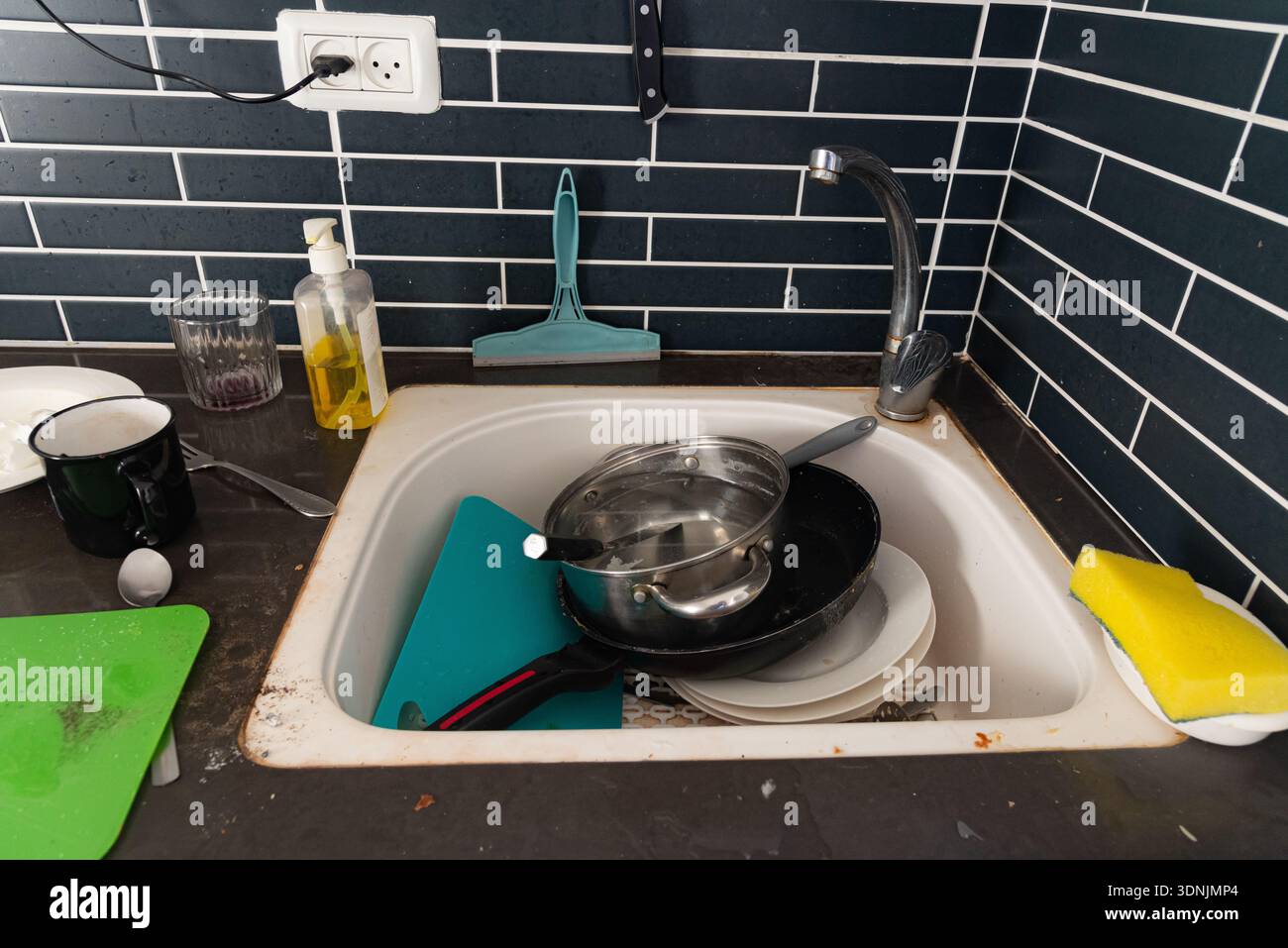 Dirty kitchen sink filled with unwashed dishes, utensils and cleaning ...