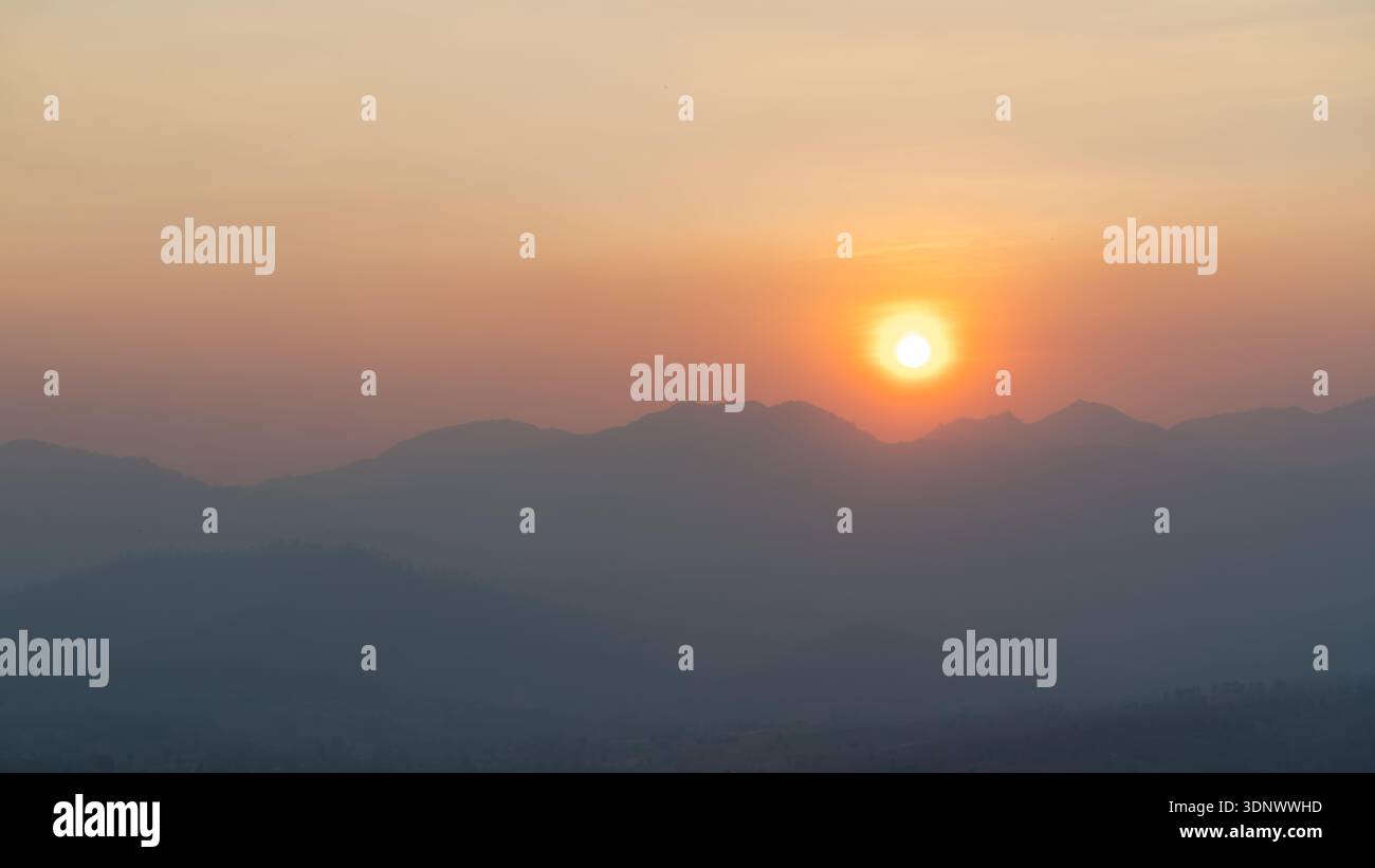 A hazy sunset over layered mountain ridges during burning season in Pai ...
