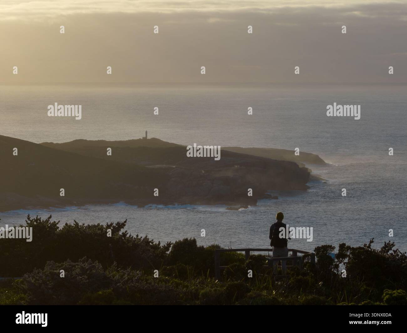 A lone, unidentifiable person stands at a lookout overlooking rugged ...