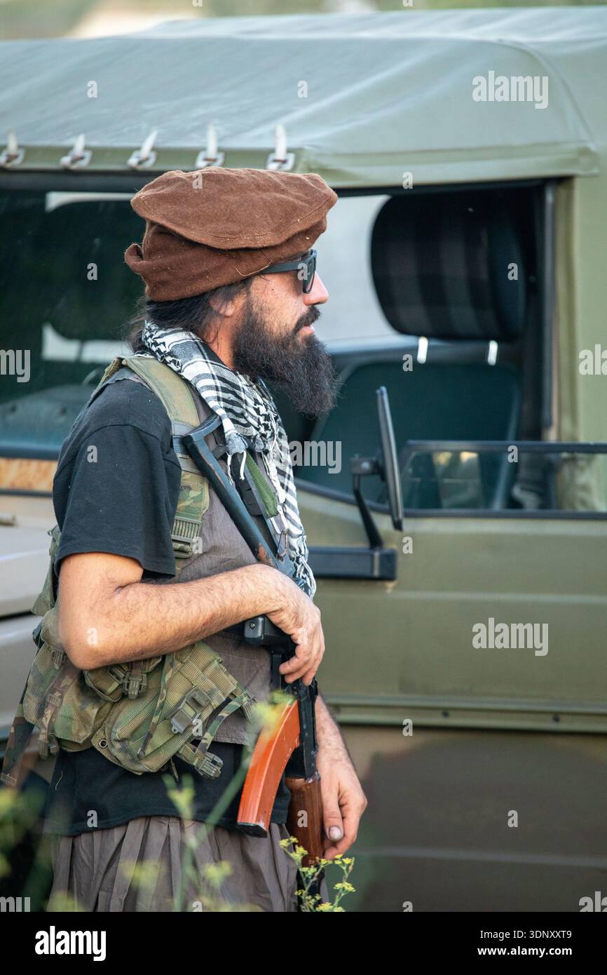 A bearded man wearing tactical military gear stands near a vintage army ...