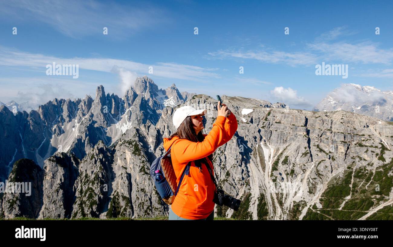 A woman in an orange jacket and white cap captures photos with her ...