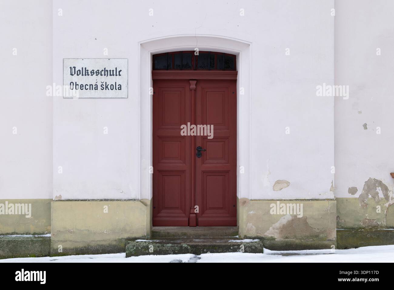 Old school building entrance with a red wooden door and dual language ...