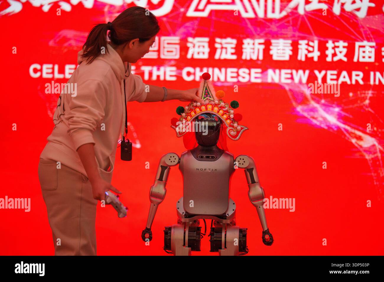 A staff member adjusts a festive headpiece on a humanoid robot during a ...