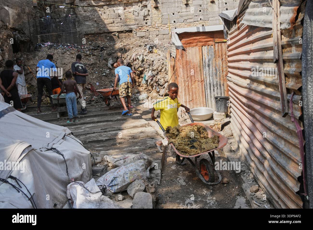 A young boy pushes a wheelbarrow of trash at a shelter for families ...