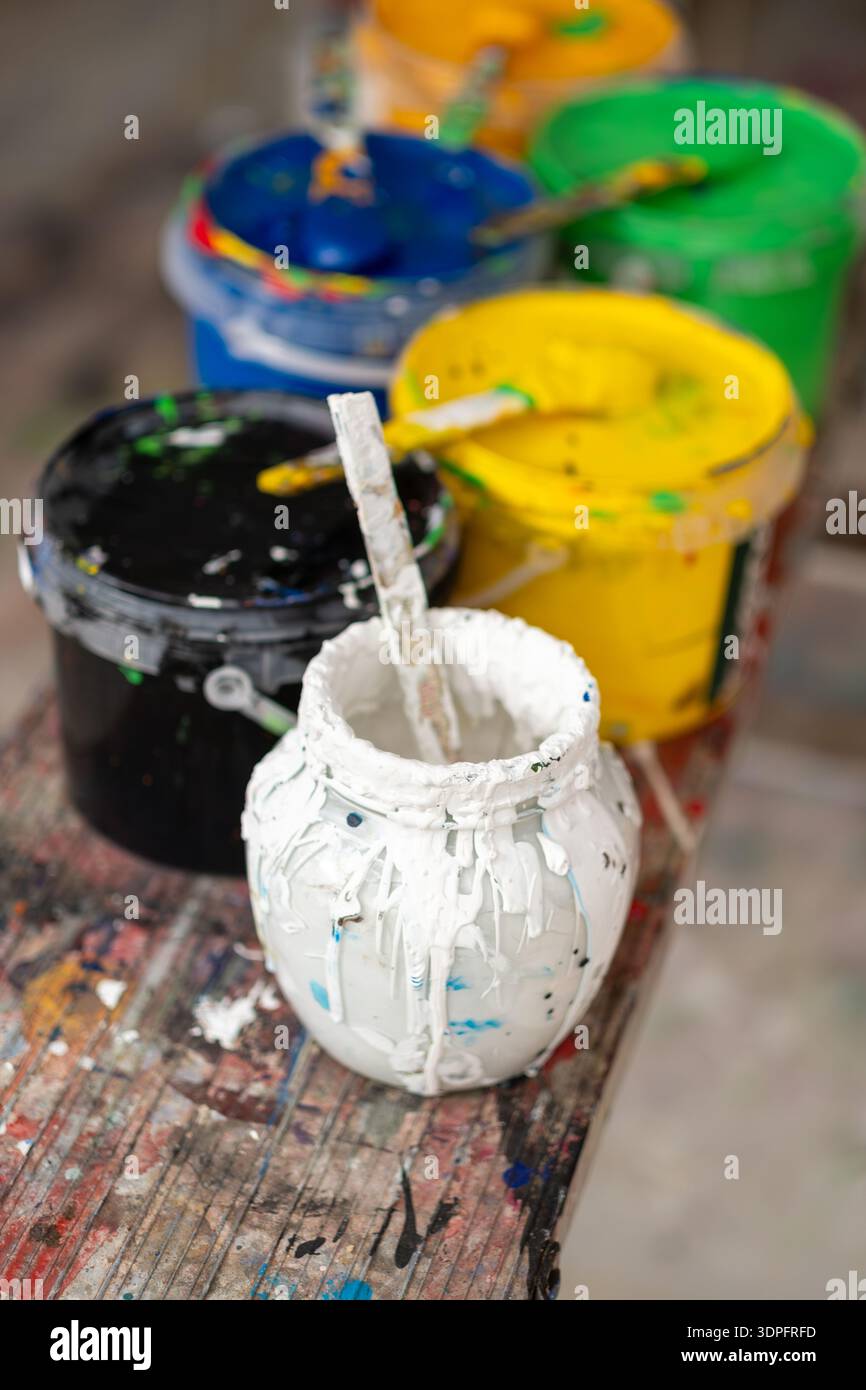 Open paint buckets in bold yellow green blue and black stand on a ...