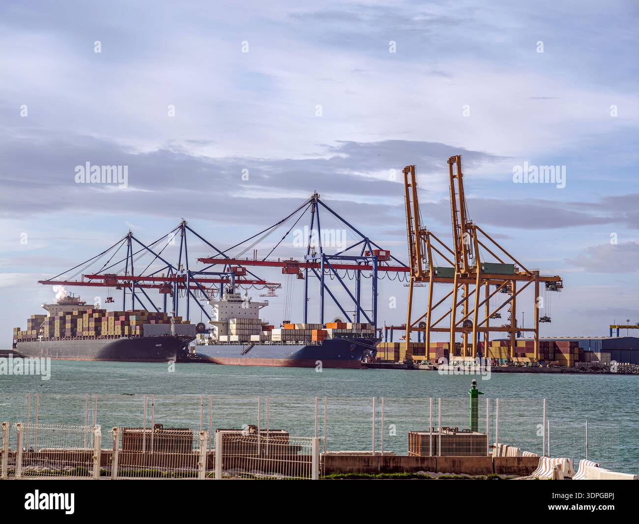 Two large cargo ships loaded with colorful containers docked at a busy ...