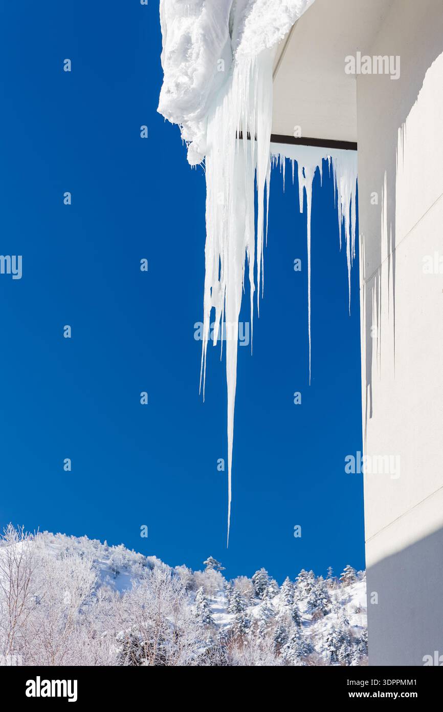 Long sharp icicles formed on a building eave against a clear deep blue ...