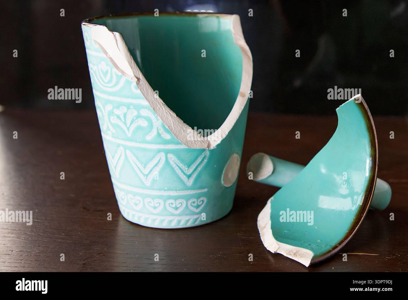 Broken turquoise ceramic cup with handle pieces on wooden table surface ...