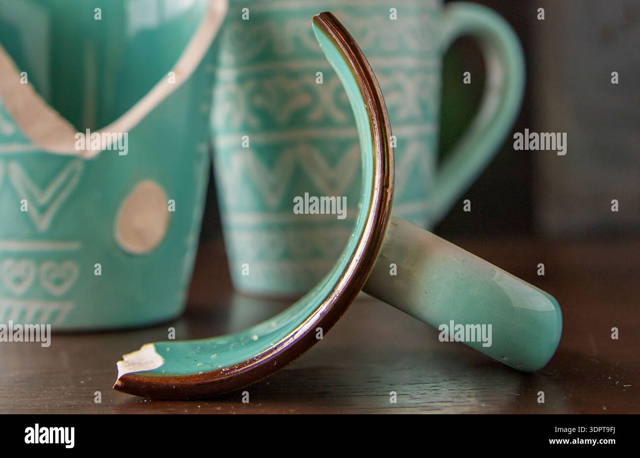 Broken turquoise ceramic cup with handle pieces on wooden table surface ...