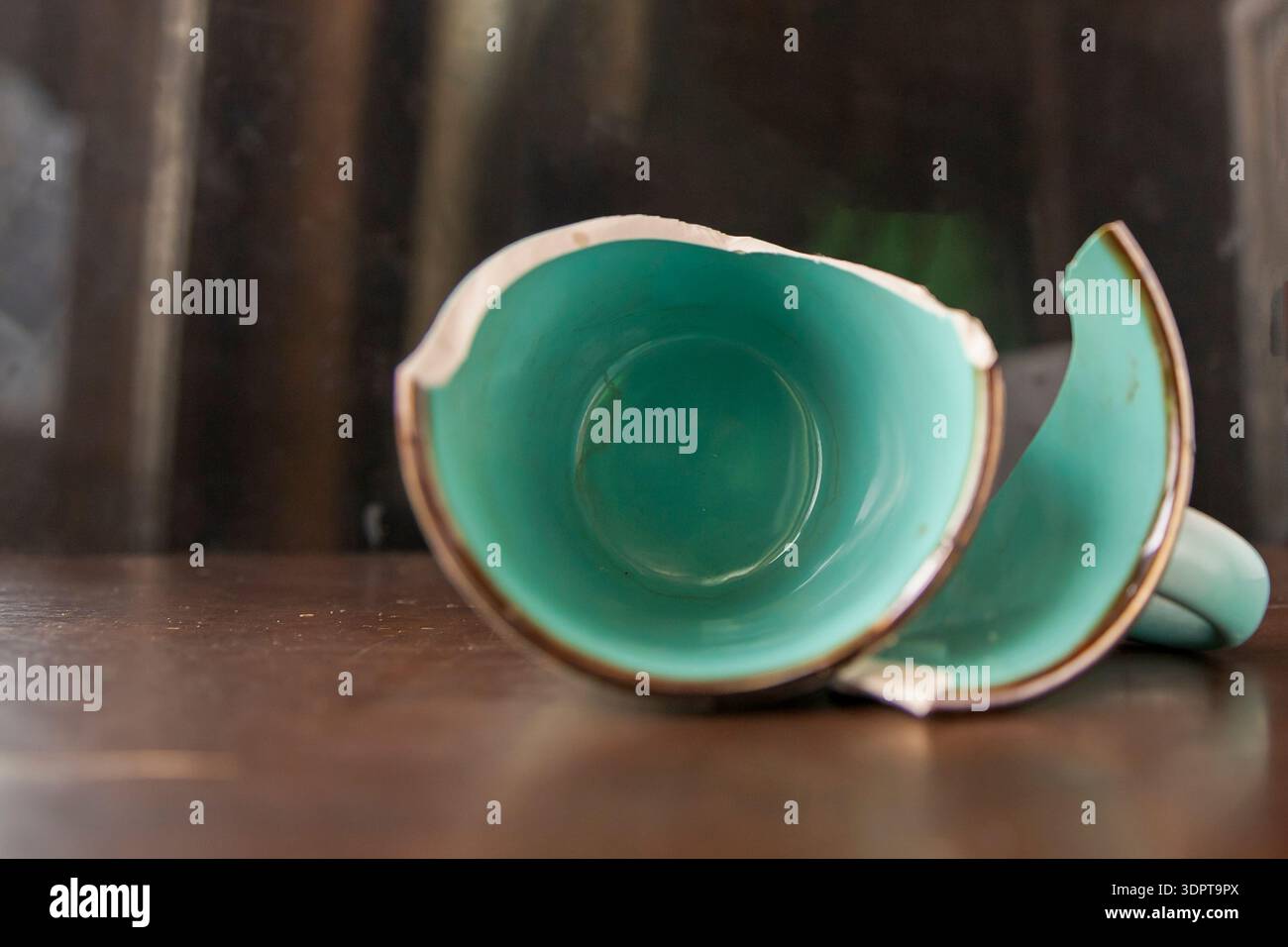 Broken turquoise ceramic cup with handle pieces on wooden table surface ...