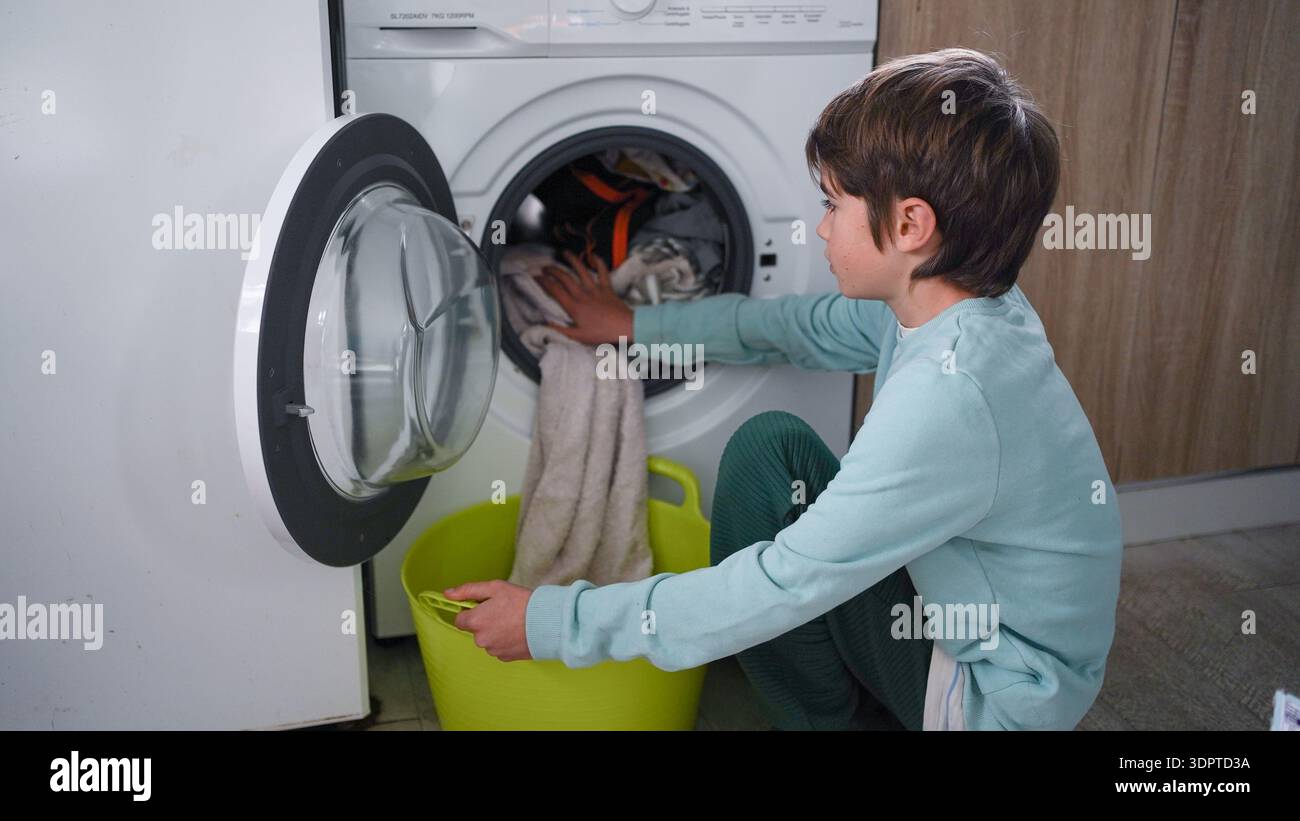 Young boy loading dirty laundry into a front-loading washing machine ...