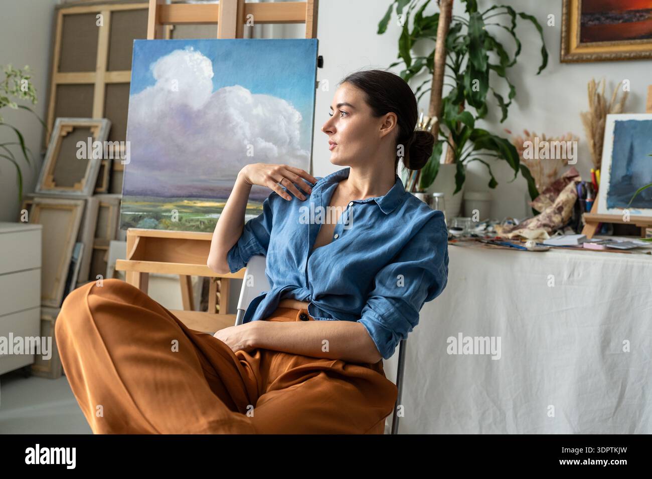Thoughtful tranquil female artist sitting in chair looking at window ...