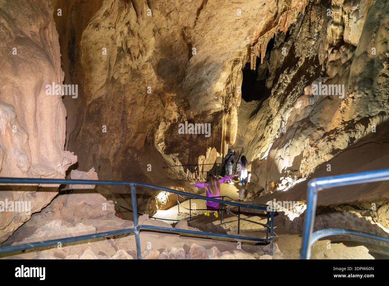 A group of people are walking through a cave with a blue railing. The ...